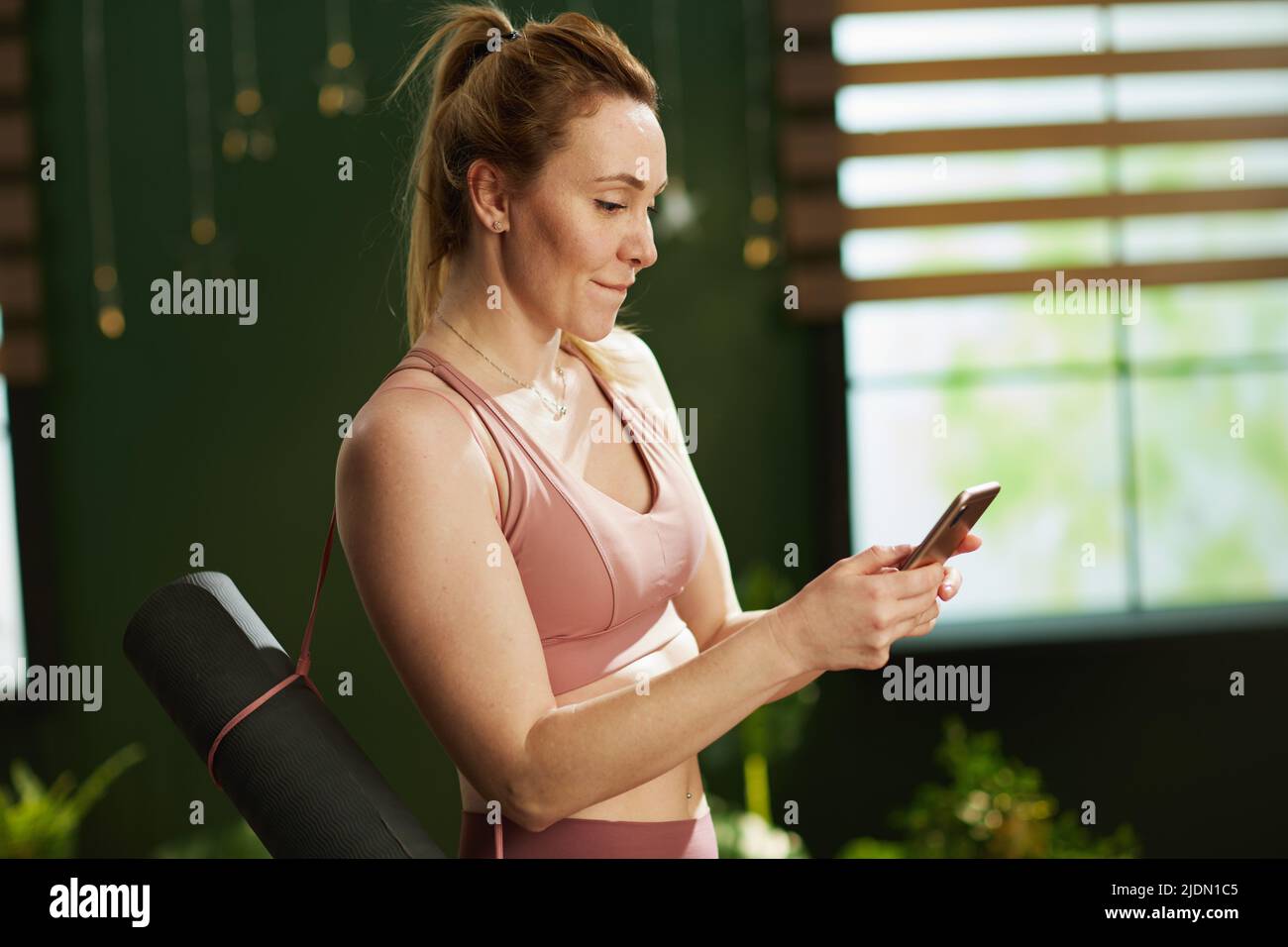 modern middle aged woman with yoga mat using smartphone at modern green ...