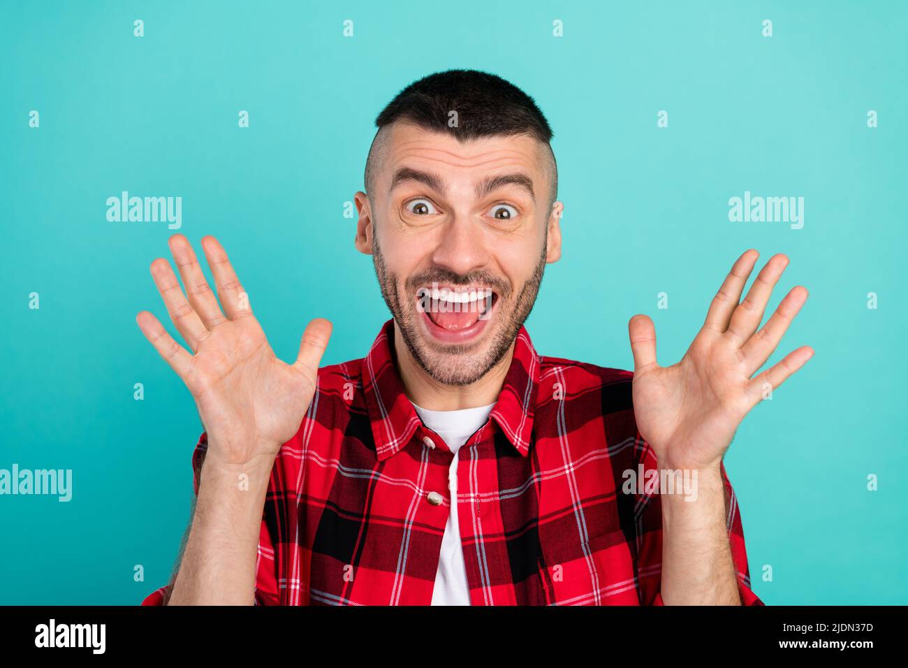 Photo of impressed millennial brunet guy hands up wear checkered shirt ...