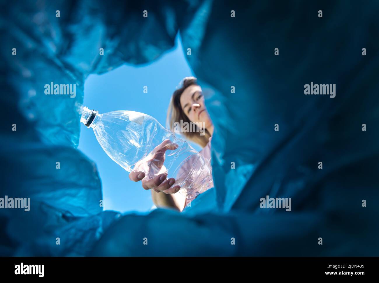 A woman throws a plastic bottle into the trash. Close-up from inside ...
