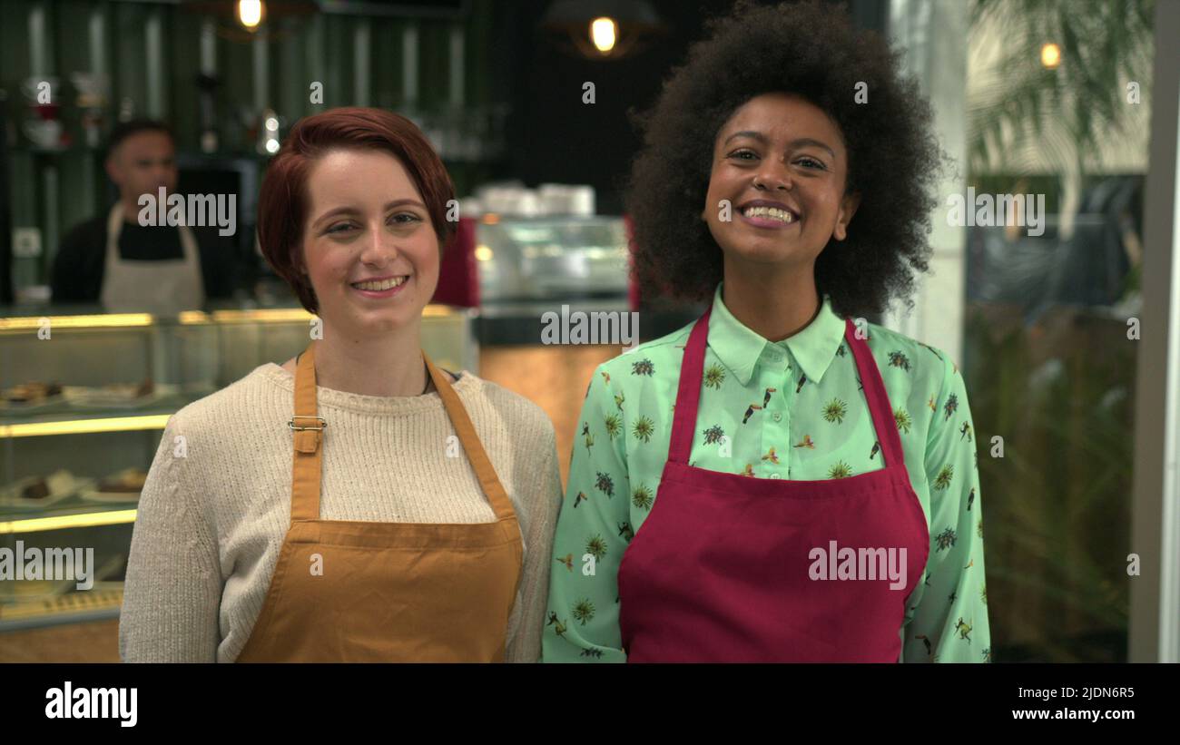 Cafe staff portrait smiling. Two happy female workers standing inside ...