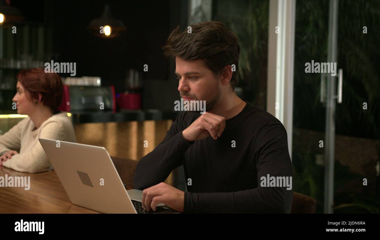 Concentrated man using laptop inside coffee shop checking smartphone ...
