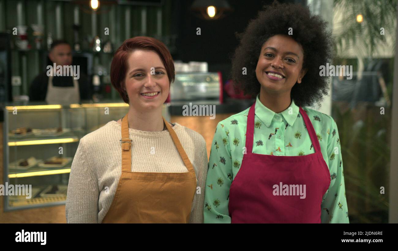 Cafe staff portrait smiling. Two happy female workers standing inside ...