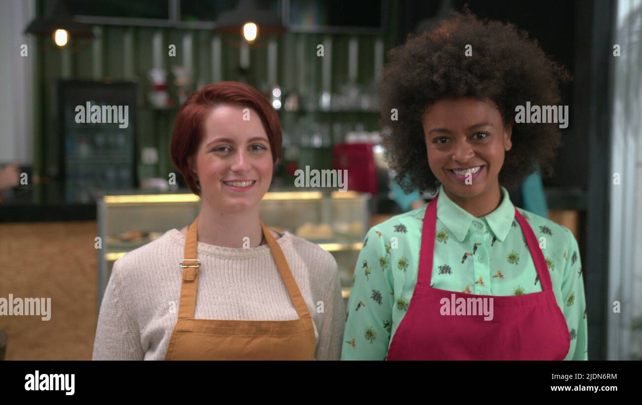 Portrait of two women baristas in aprons in cafe. Young employees at ...