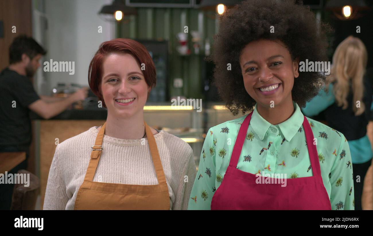Portrait of two women baristas in aprons in cafe. Young employees at ...