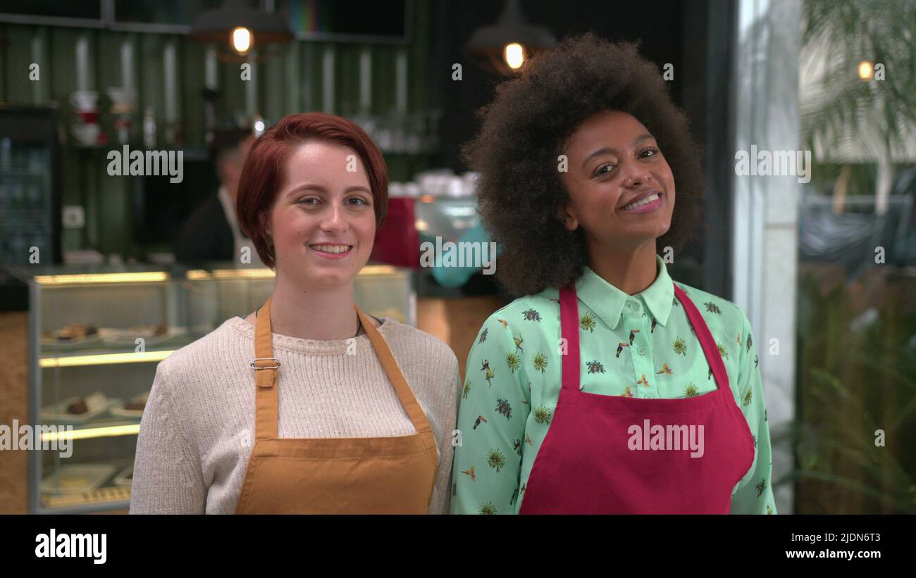 Portrait of two women baristas in aprons in cafe. Young employees at ...