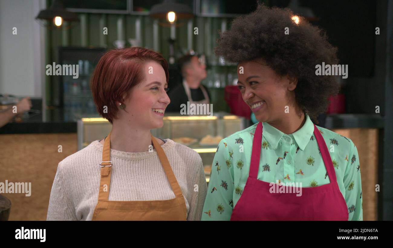 Portrait of two women baristas in aprons in cafe. Young employees at ...