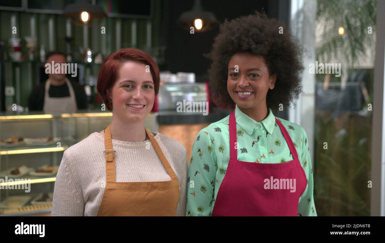Portrait of two women baristas in aprons in cafe. Young employees at ...