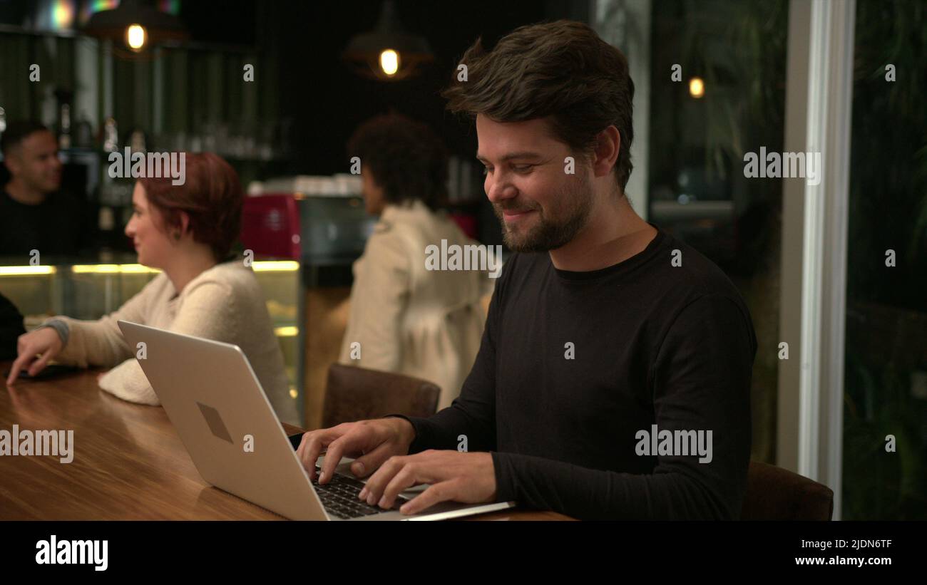Young entrepreneur working at night in front of laptop inside cafe ...