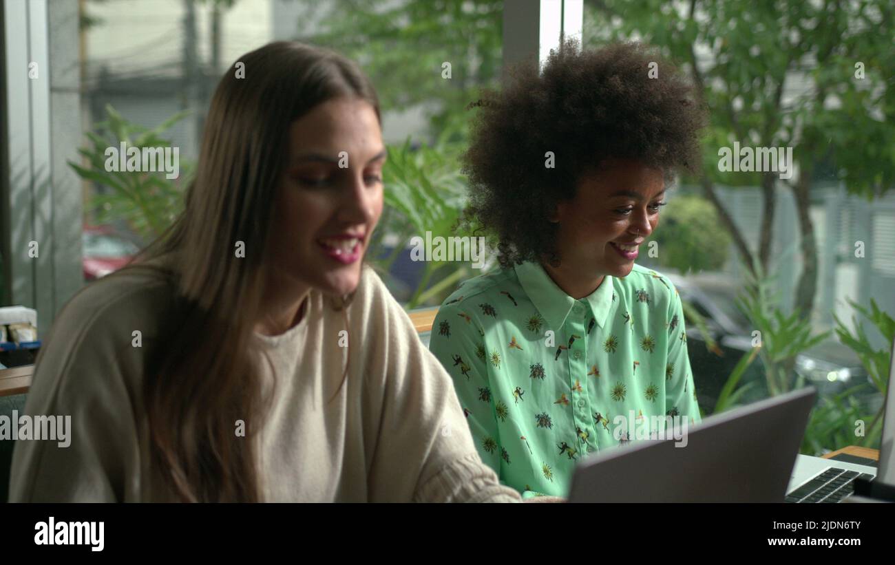 Two diverse female colleagues working remotely at coffee shop in front ...