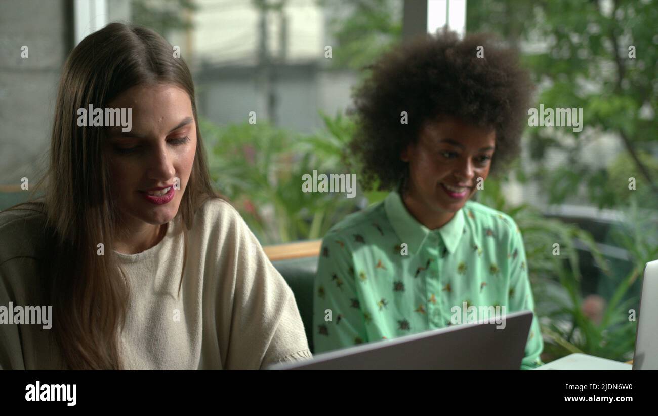 Two diverse female colleagues working remotely at coffee shop in front ...