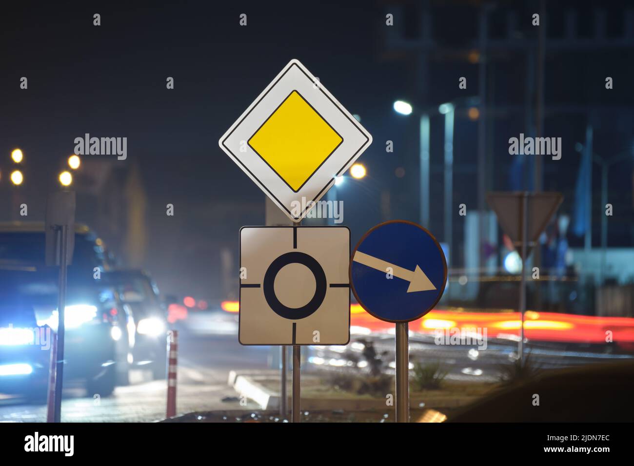 Roundabout road signs with blurred cars on city street traffic at night ...