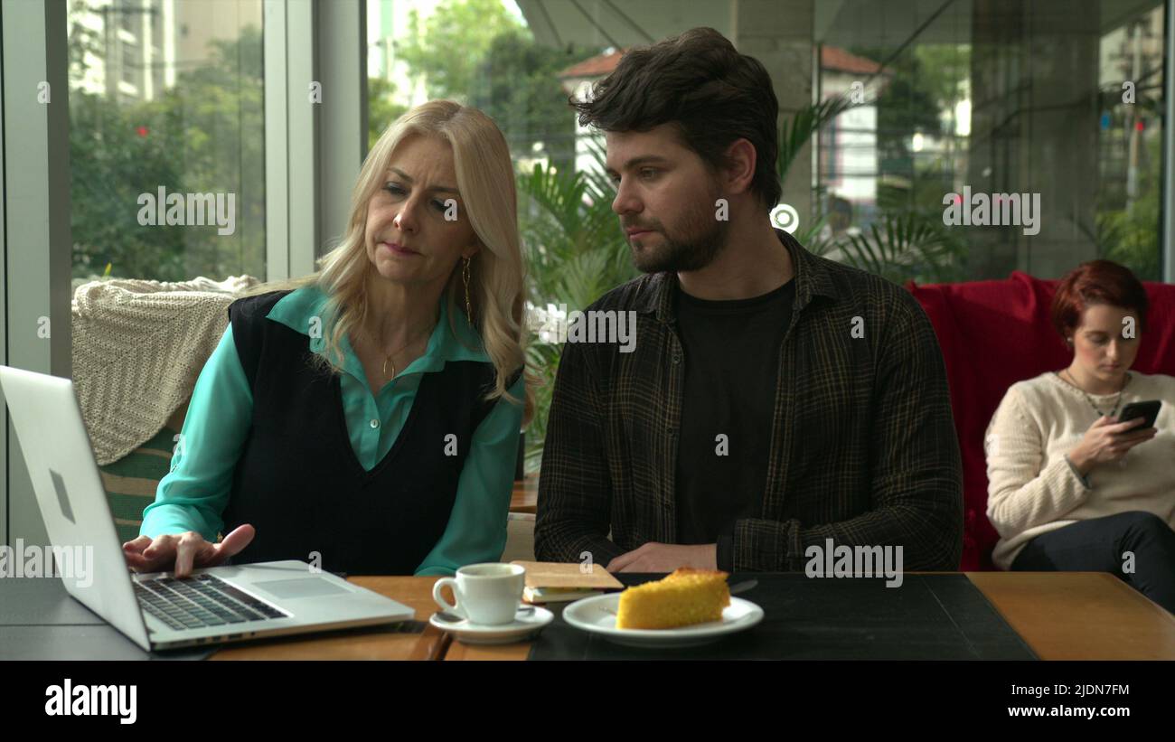 Female leader coaching younger man in front of computer laptop at cafe ...