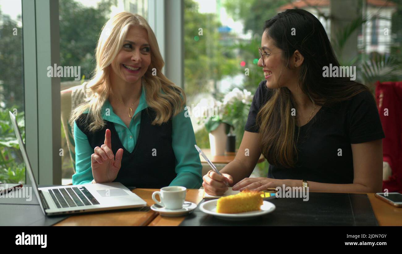 Female leader coaching younger man in front of computer laptop at cafe. Woman explaining ...