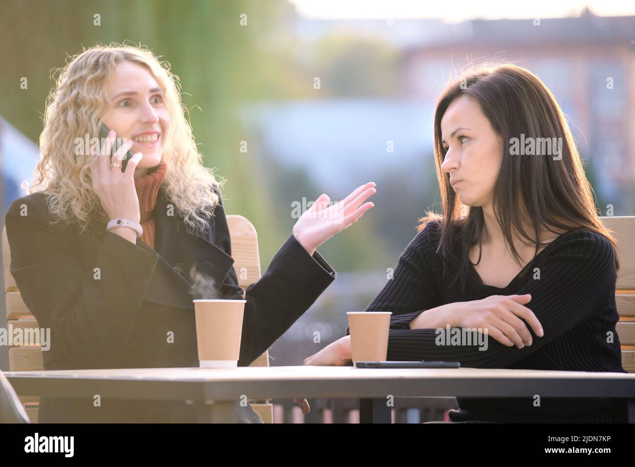 Sad woman being ignored by her friend sitting at street cafe outdoors ...