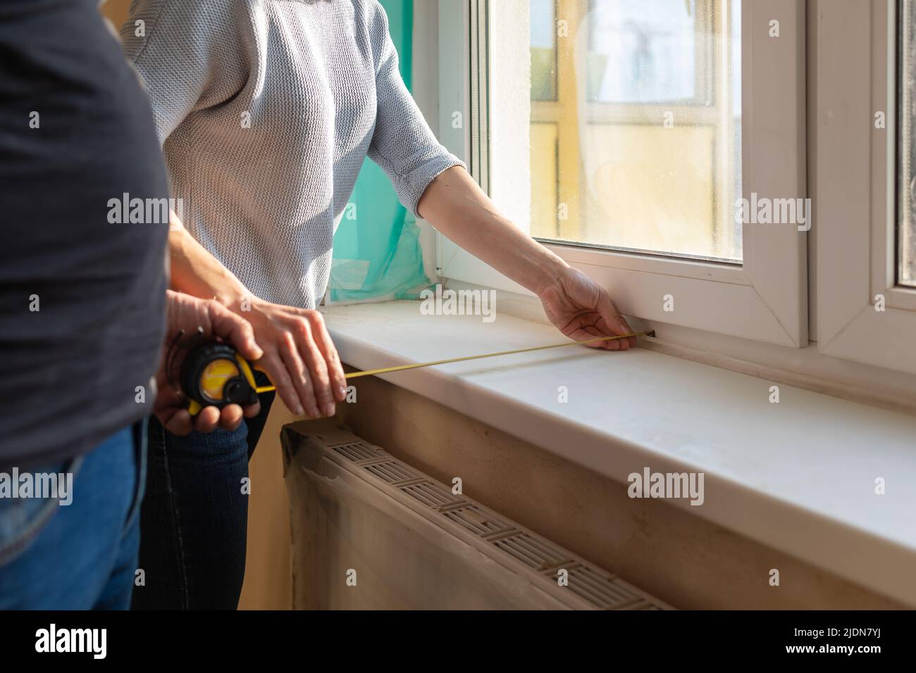 Young couple moving in new apartmen. People measure size of window sill ...