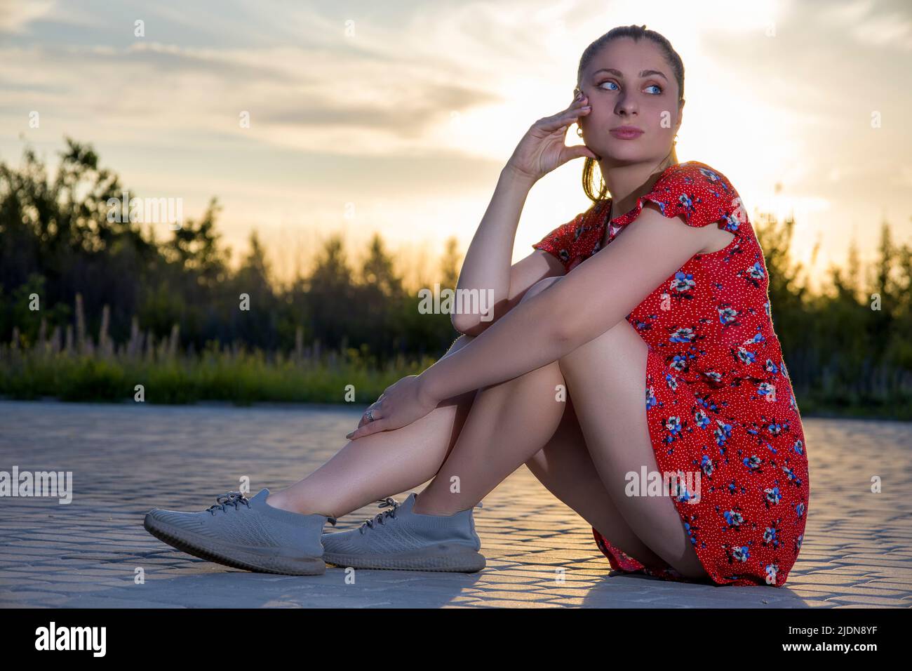 Beautiful girl with blue eyes and in a red dress sitting on the ground ...