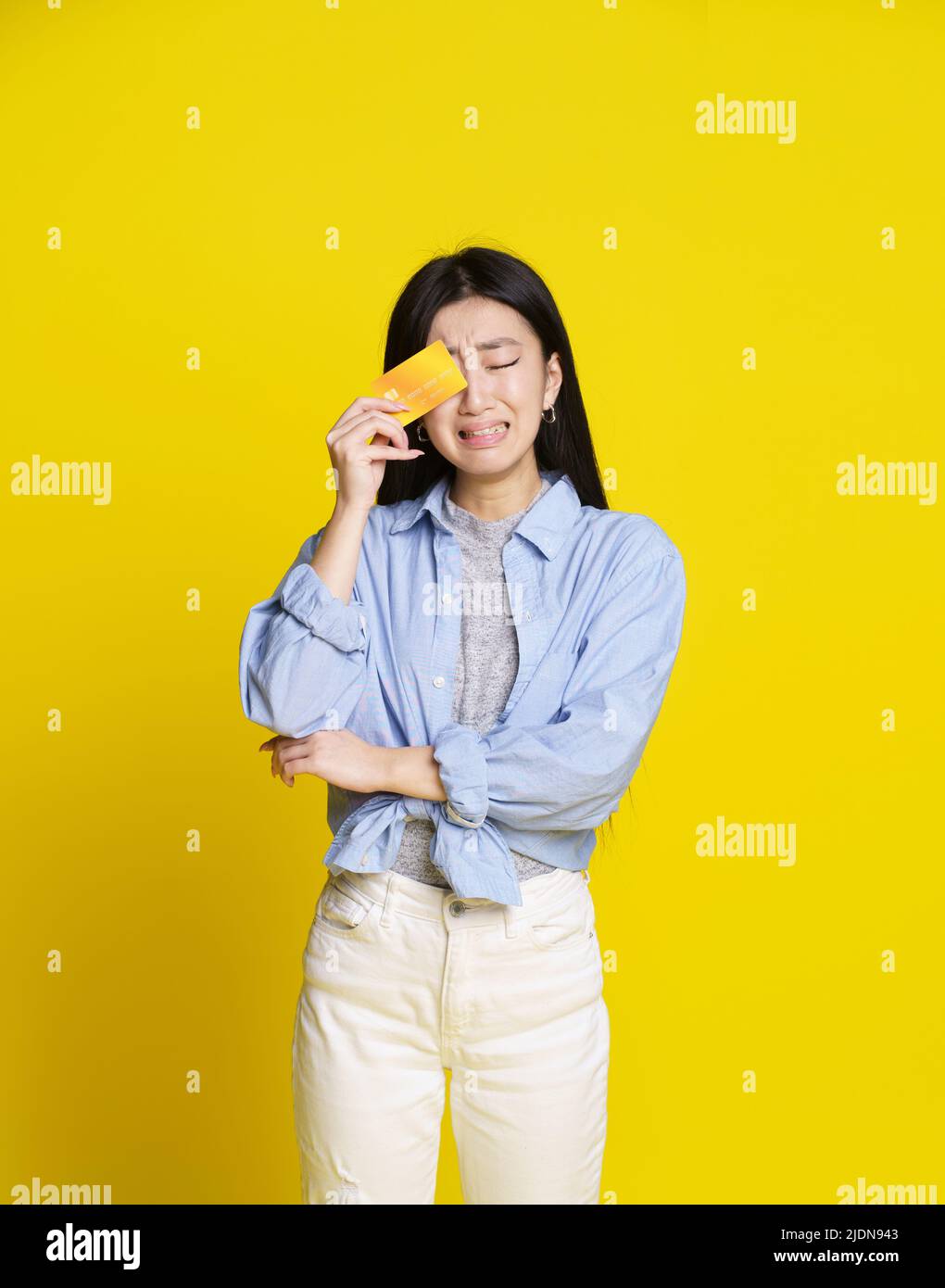 Unhappy, broke crying asian girl holding yellow credit, debit card next ...