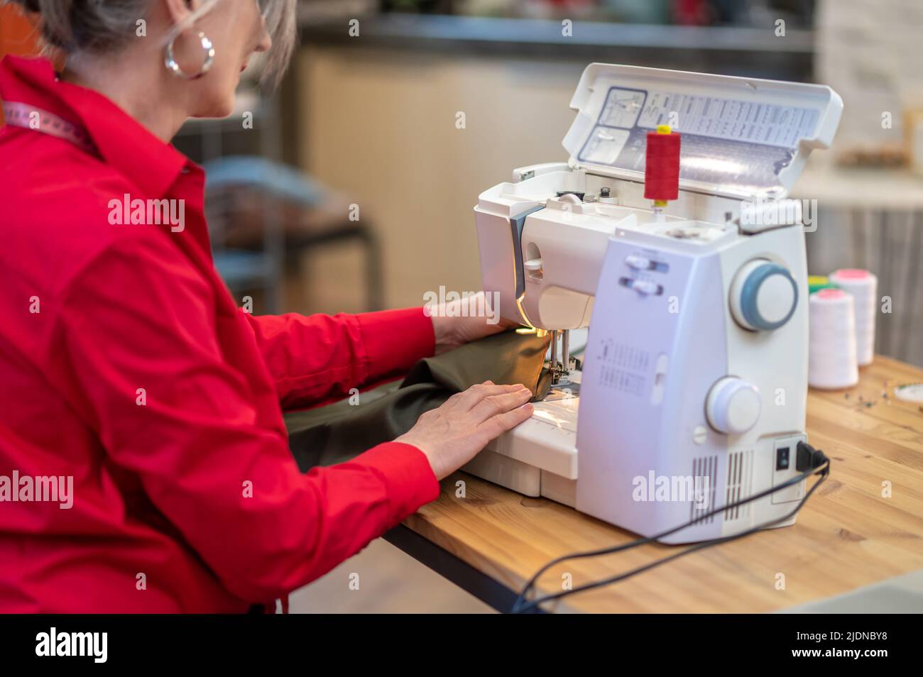 Woman sewing on machine sideways to camera Stock Photo - Alamy