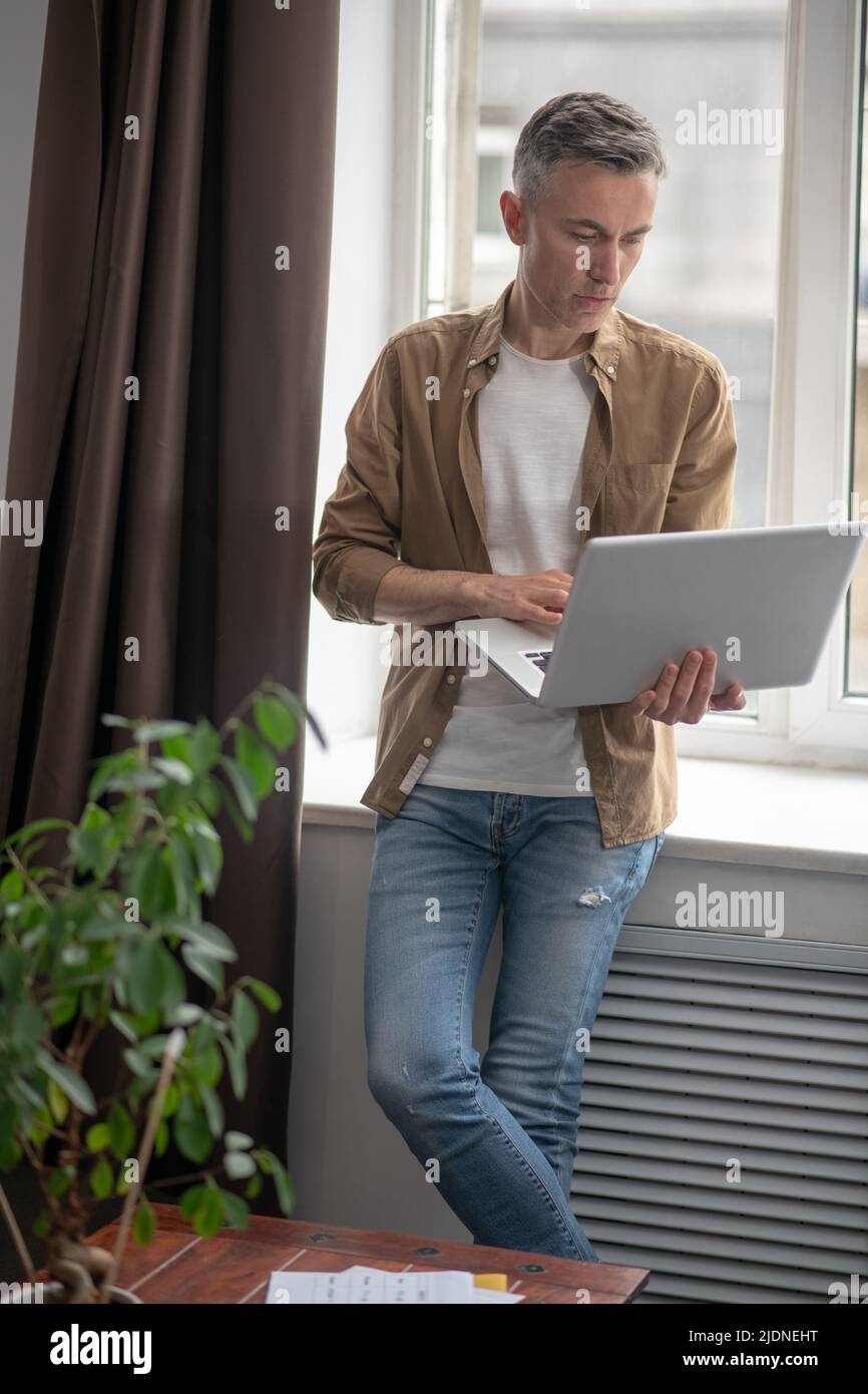 Man standing holding laptop looking at screen Stock Photo - Alamy