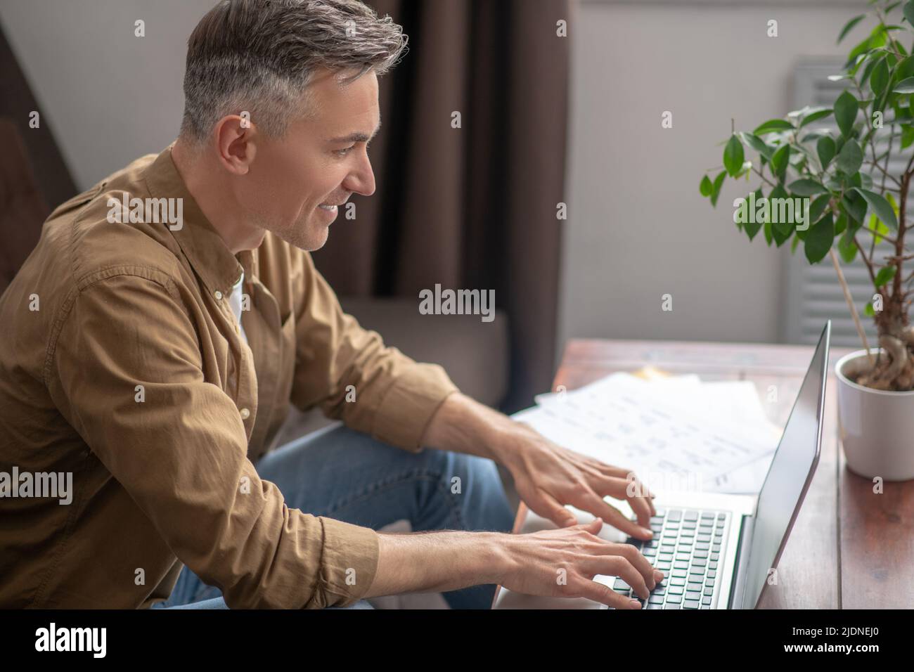 Man typing smiling at laptop screen Stock Photo - Alamy