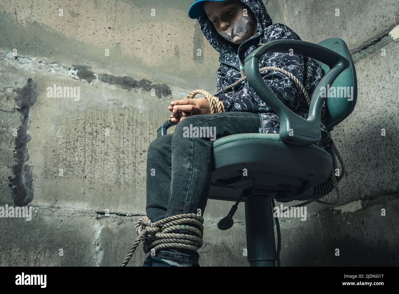 a child in the basement is sitting on a chair tied with a rope Stock ...