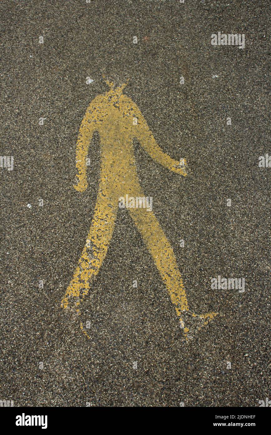 faded and worn yellow man symbol painted on the tarmac of the footpath ...