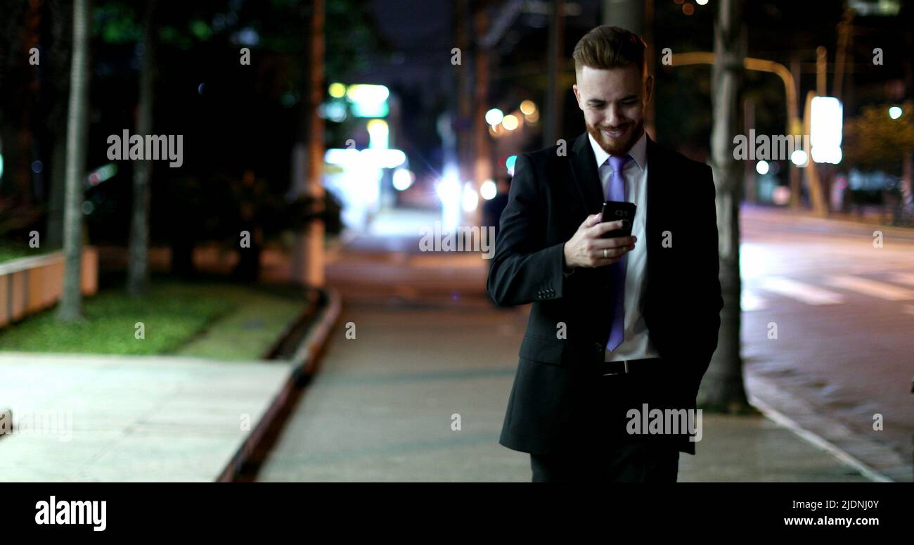 Business man looking at cellphone device at night walking on sidewalk ...
