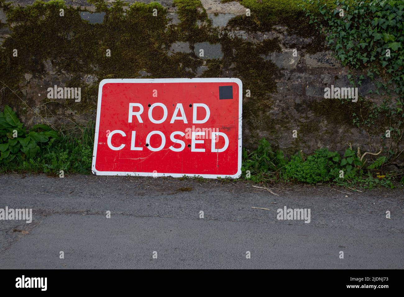 white and red road closed sign leaning against an old stone wall with ...