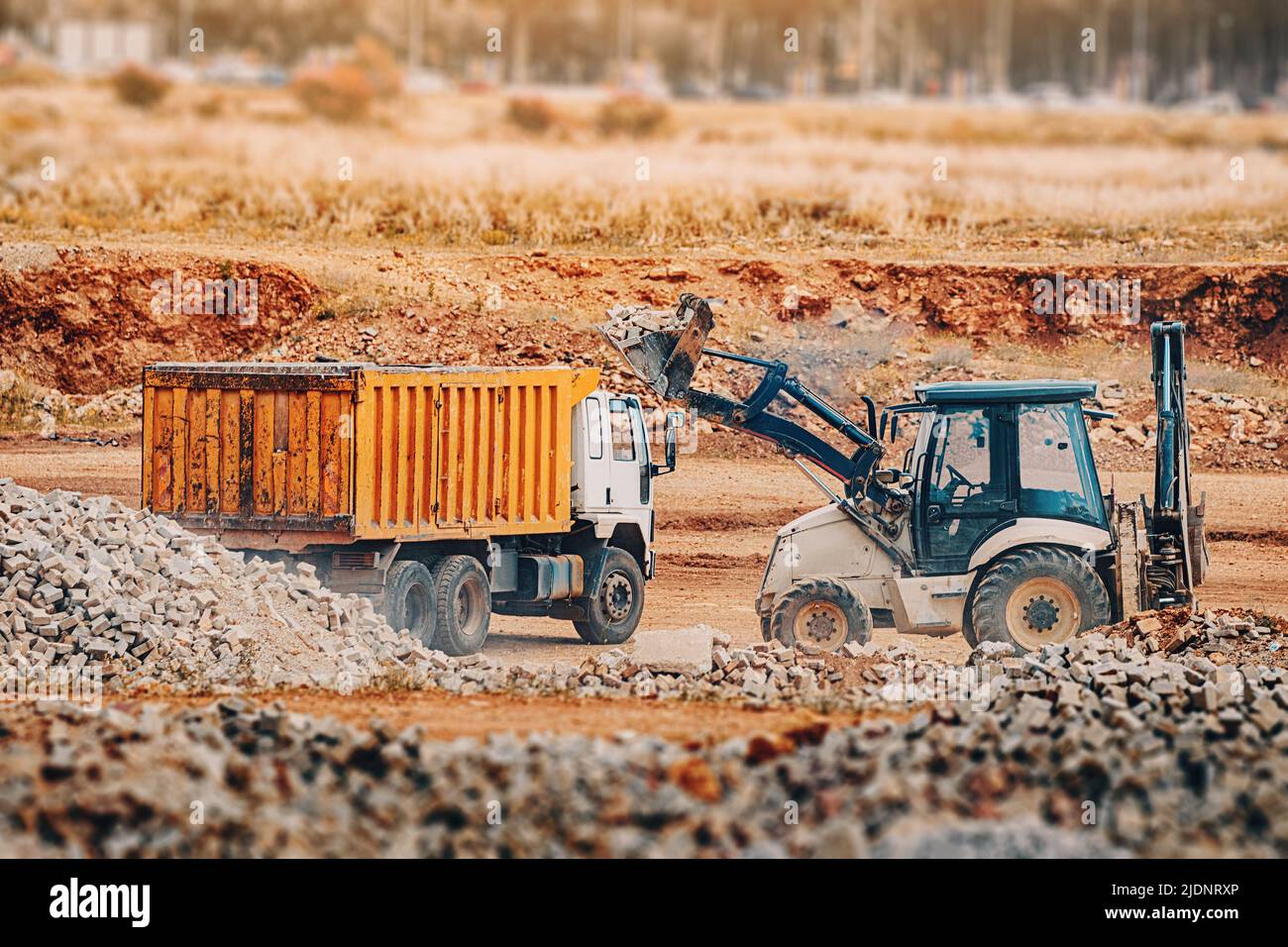 a tractor loads bricks and other construction debris with a bucket into ...