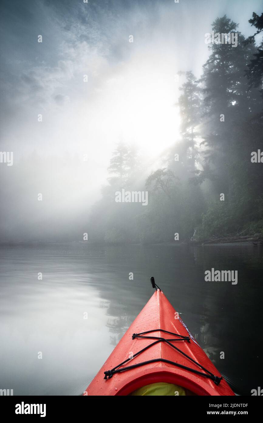 Bright red kayak slips through the morning mist on the calm water of ...