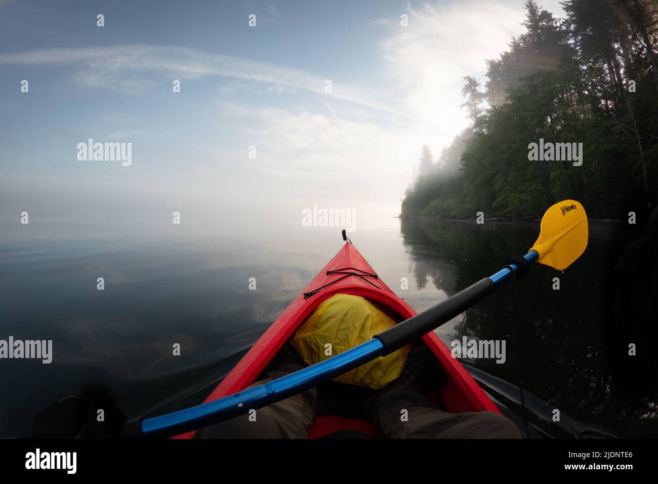 Bright red kayak slips through the morning mist on the calm water of ...