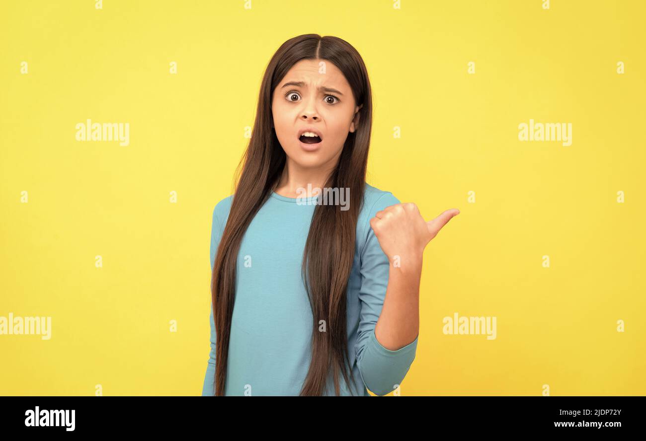 confused kid with long hair point finger on copy space on yellow ...