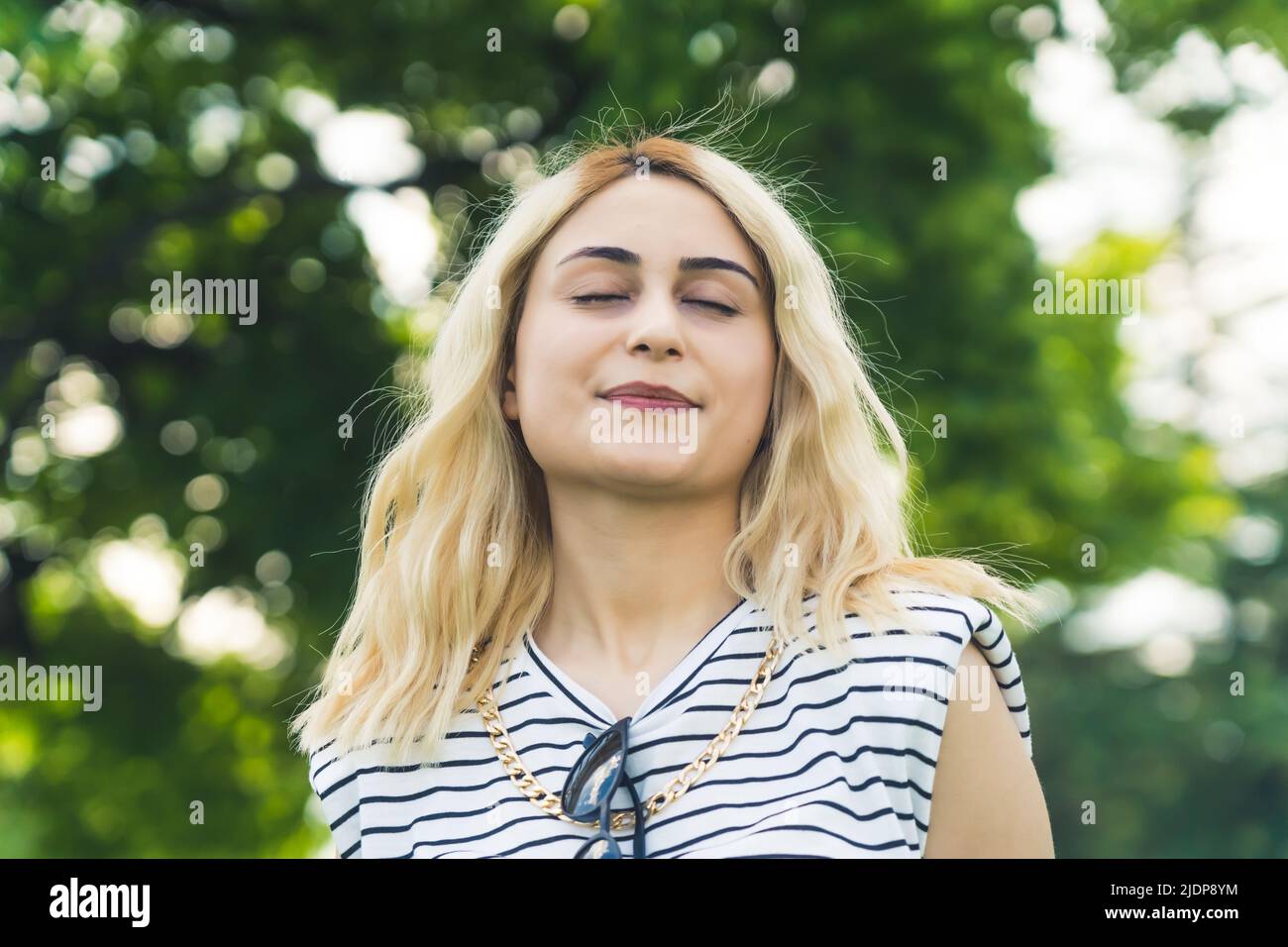 blond Caucasian girl enjoying the fresh air with closed eyes. medium closeup green background ...