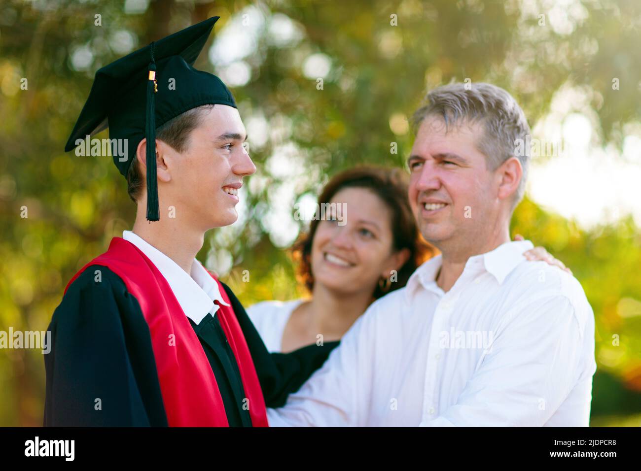 School or college graduation ceremony. Young man in gown and cap, with ...