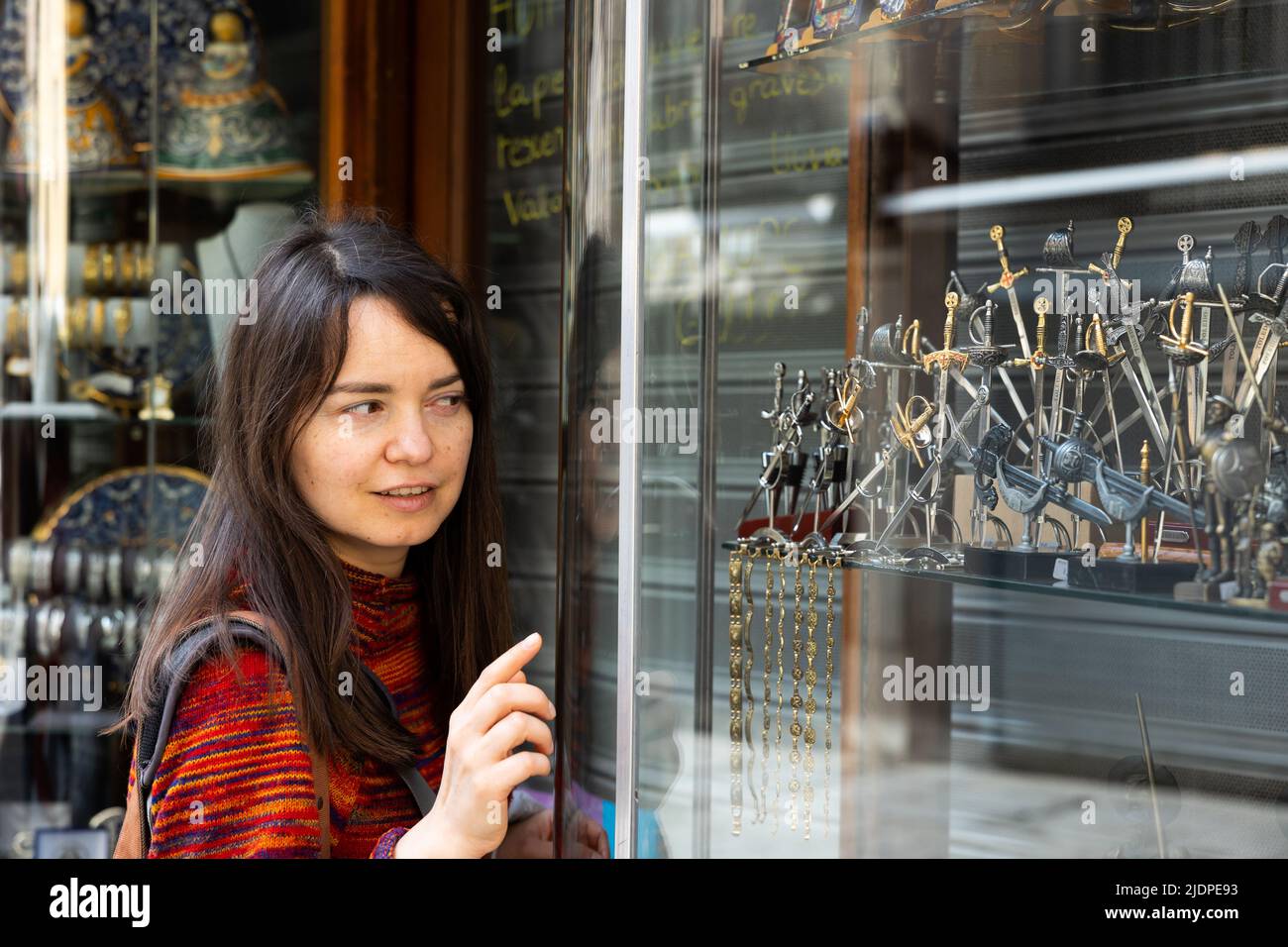 Woman tourist, standing near the window of a souvenir shop, examines ...