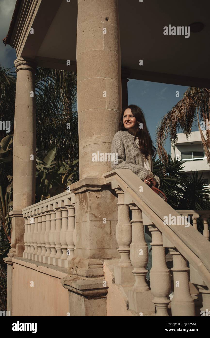 Woman stand near old building with columns and tropical plants in ...