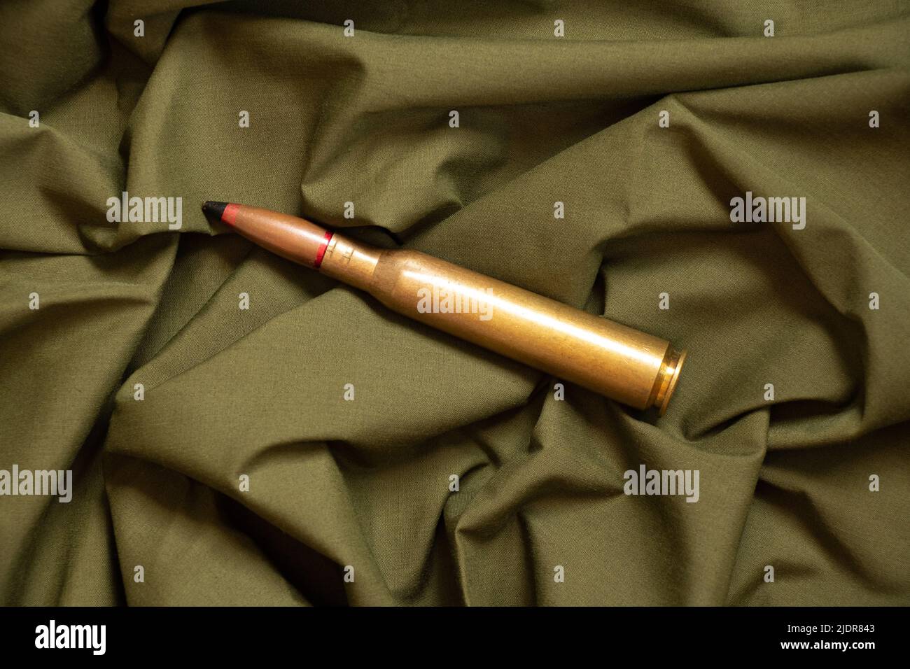 One bullet lies on a green camouflage background, military weapon ...