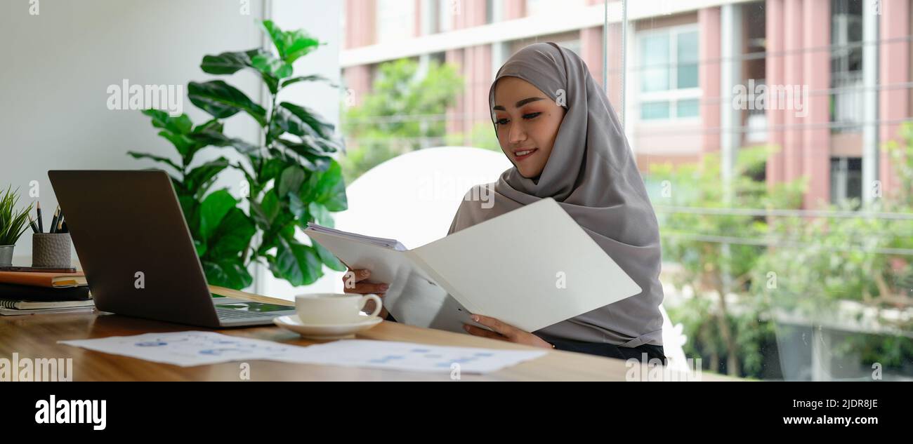Muslim woman working with laptop computer in office , writing paper ...