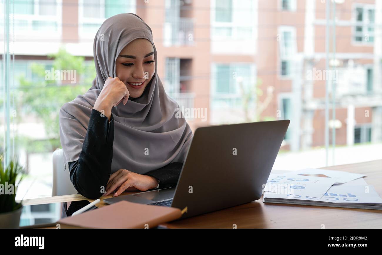 Muslim woman working with laptop computer in office , writing paper ...
