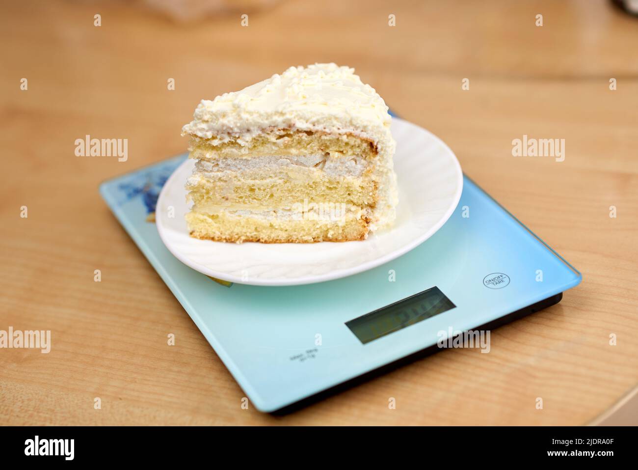 A piece of delicious cake with white butter cream lies on the scales ...