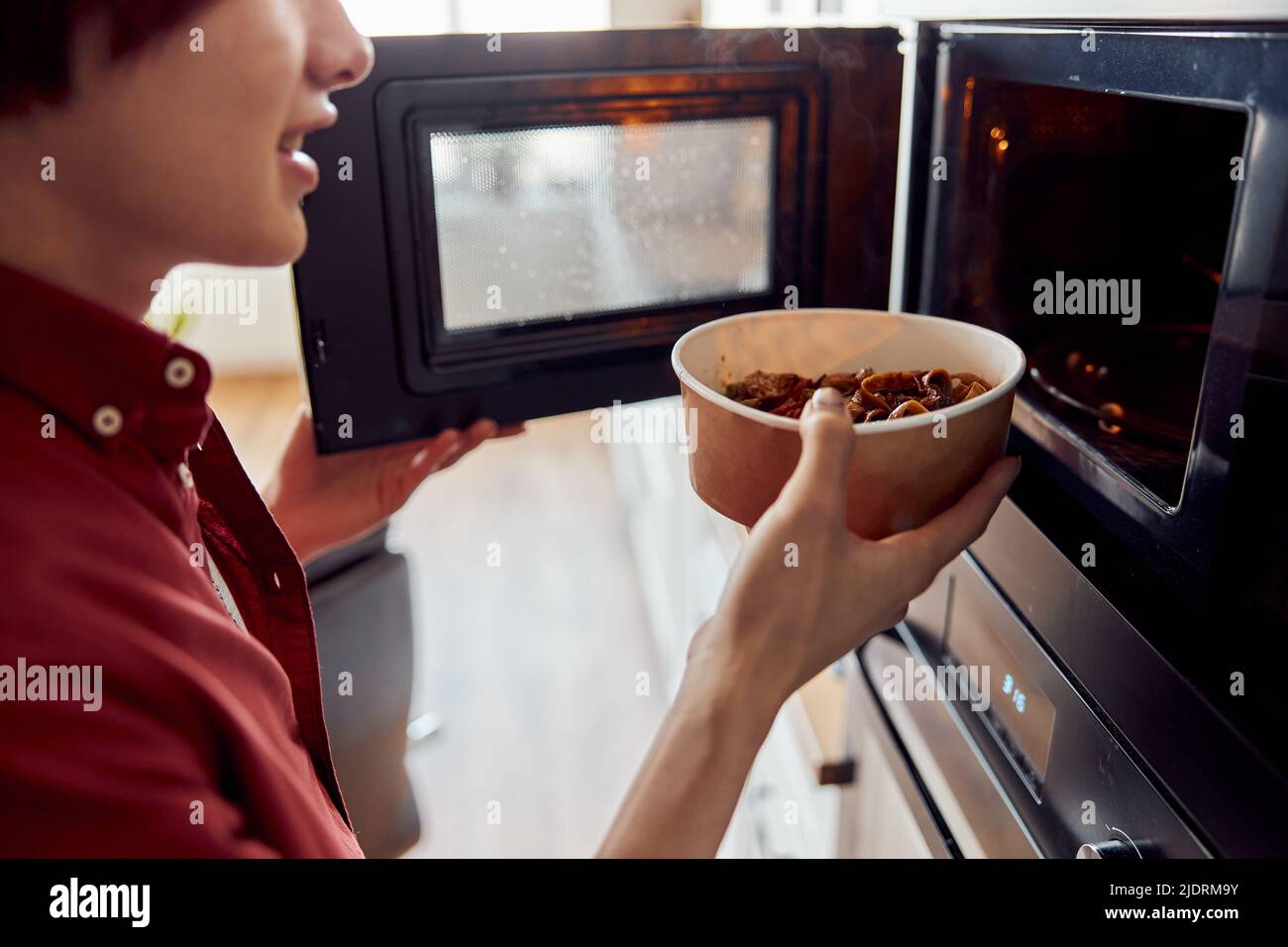 Smiling Asian guy placing a plate of food in the microwave Stock Photo ...