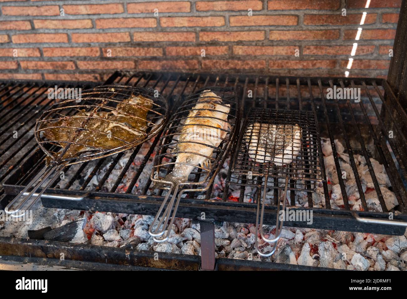 Fresh fish grilling on old charcoal parrillas white fish sea bass and ...