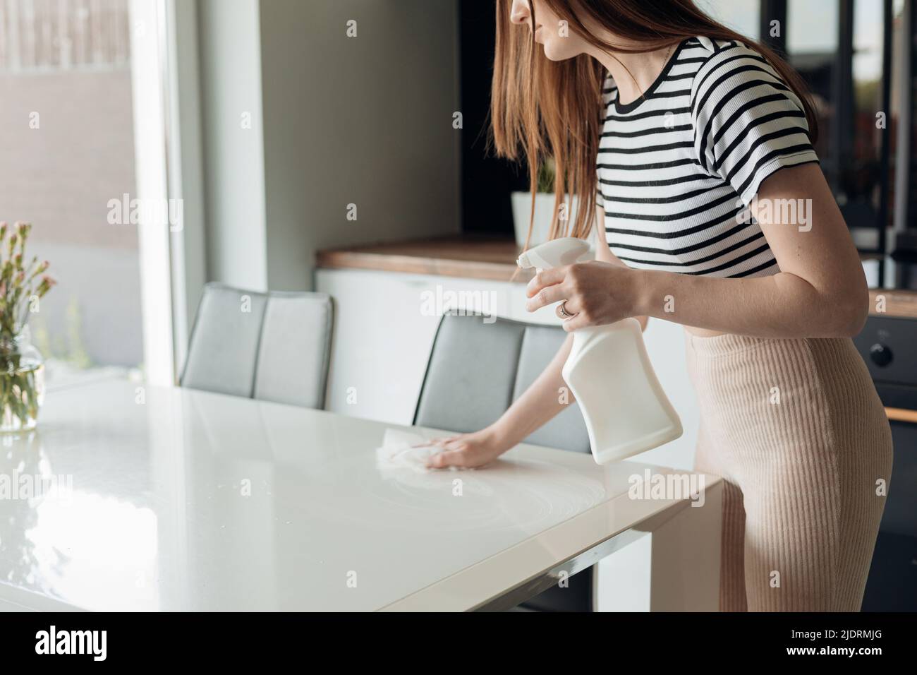 Cropped photo of young woman stand in kitchen spraying on white table ...