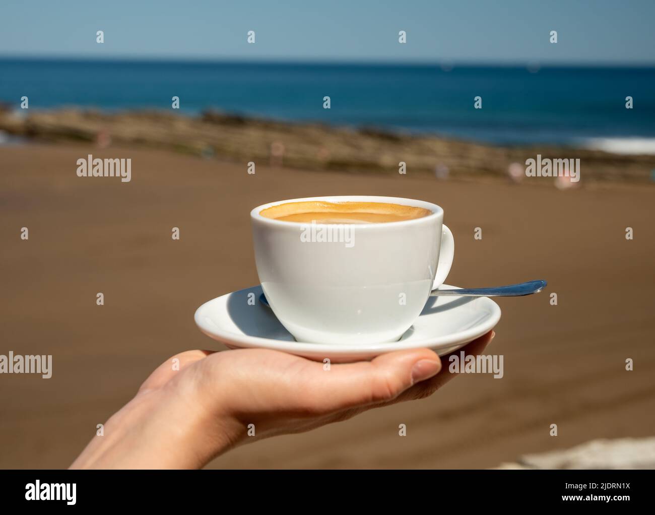 Drinking cappuccino coffee on Atlantic ocean with view on sandy beach ...