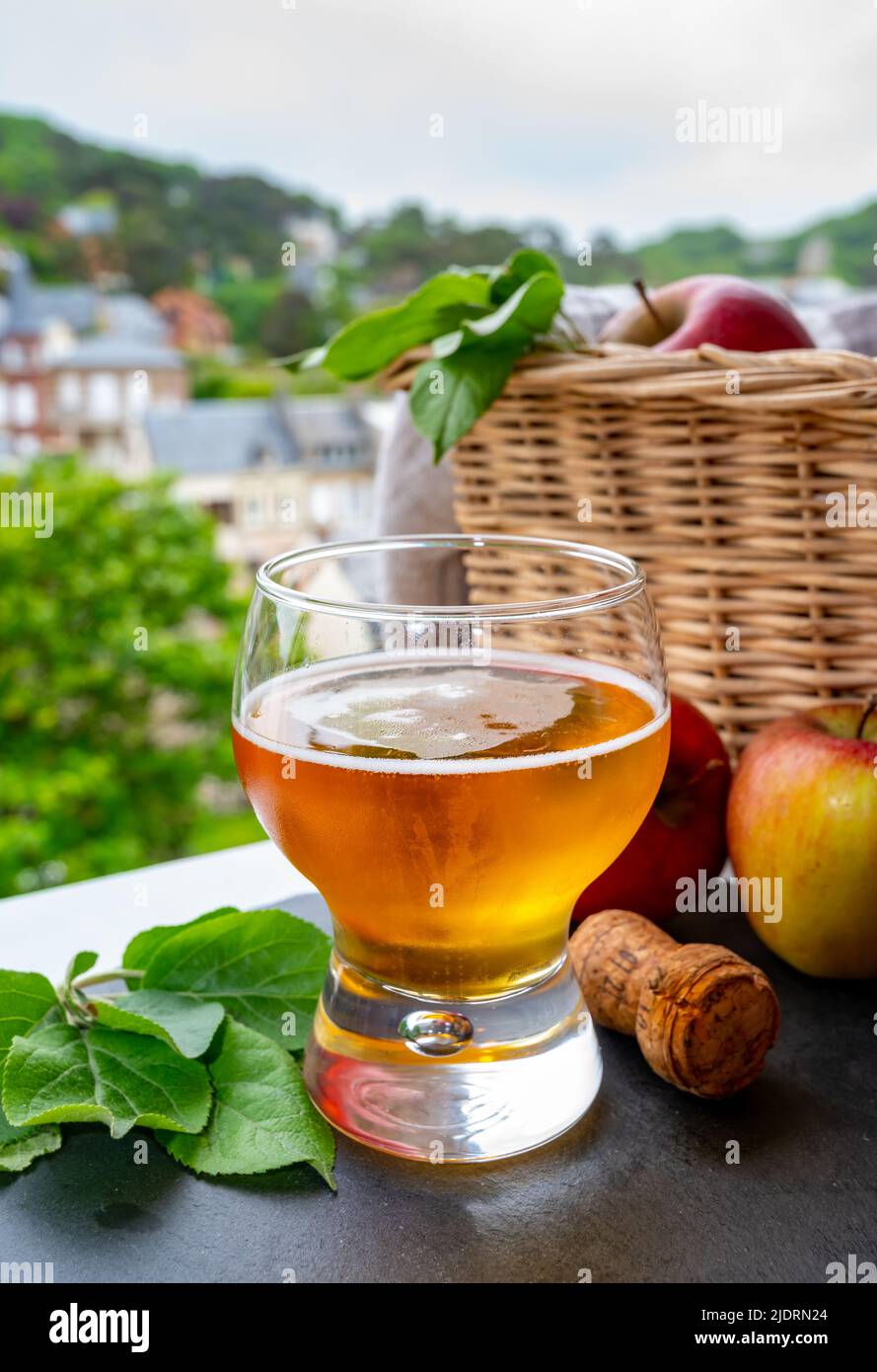 Glass of cold apple cider drink, ripe apples with leaves and houses of ...
