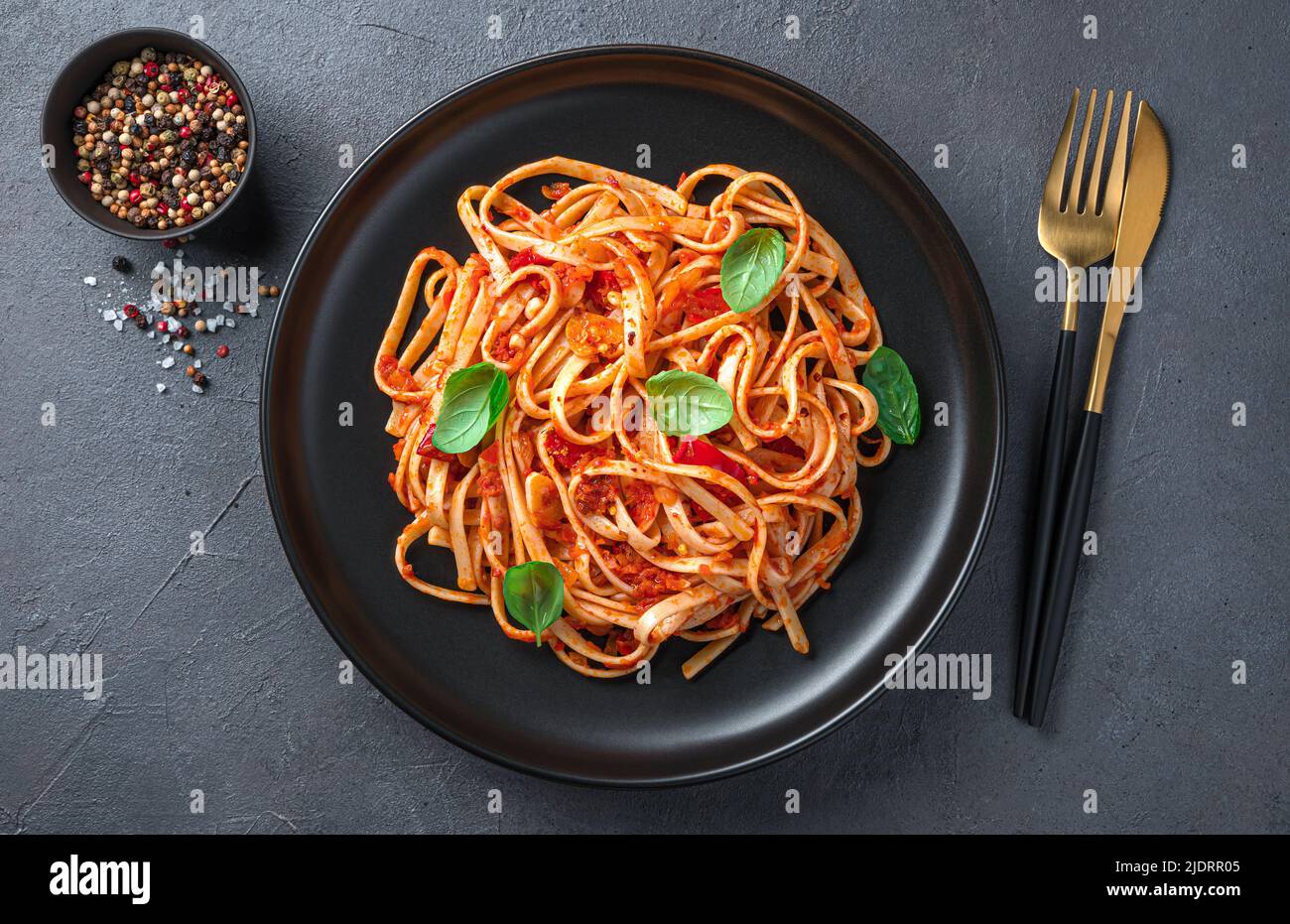 Italian linguini pasta with tomato sauce in a black plate on a dark ...
