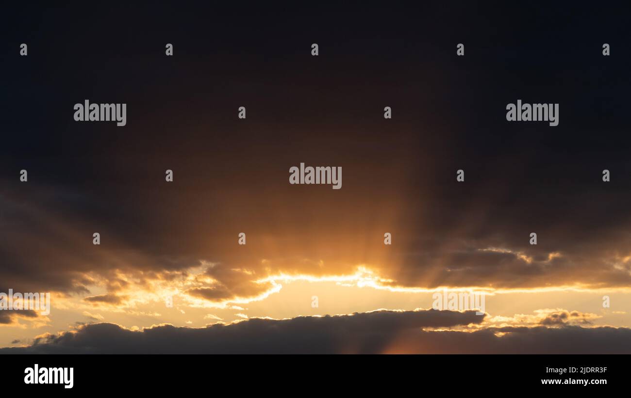 Bright sun rays coming out of gap in dark clouds at sunset, dramatic ...