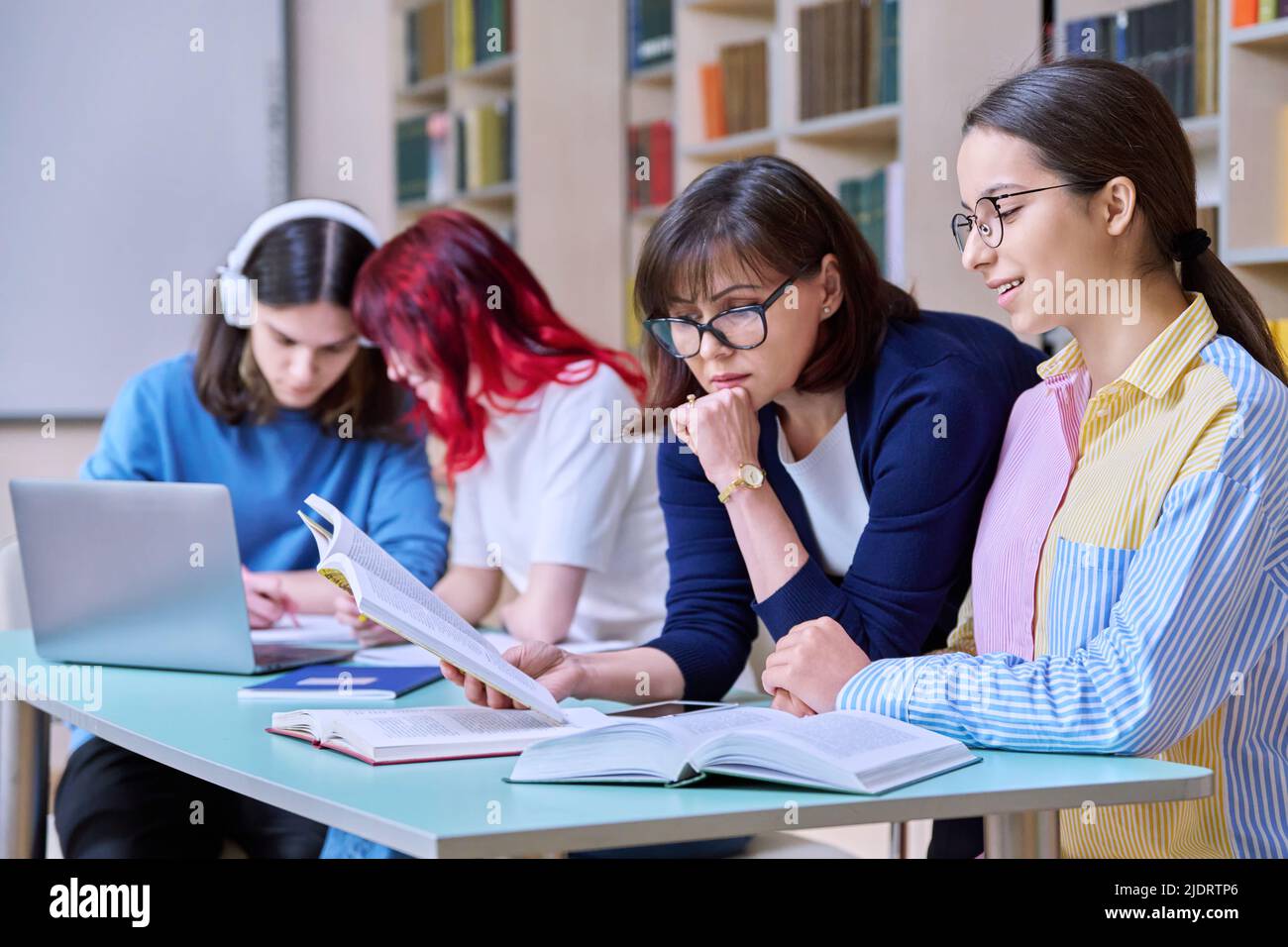 Group of teenage students and teacher study at desk in library Stock ...