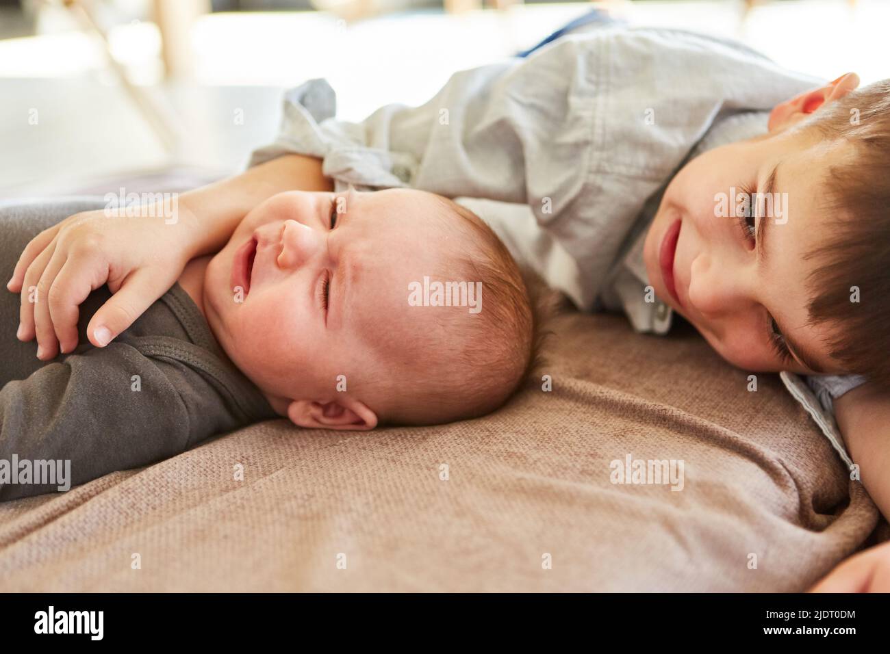 Boy as big brother comforts crying baby while cuddling together in ...
