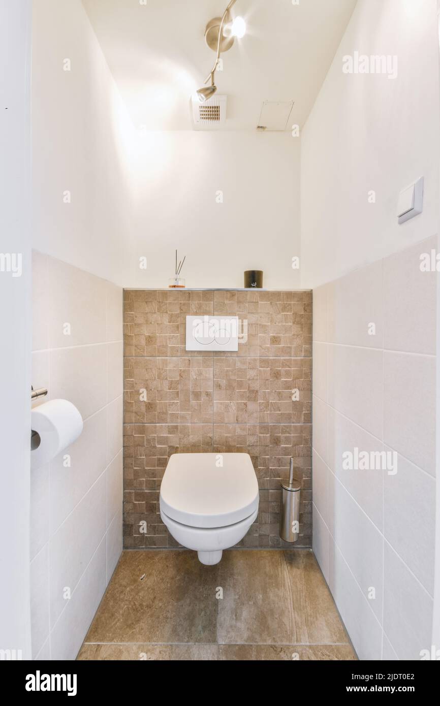 Wall hung toilet with beige white tiled walls and brown tiled floor ...